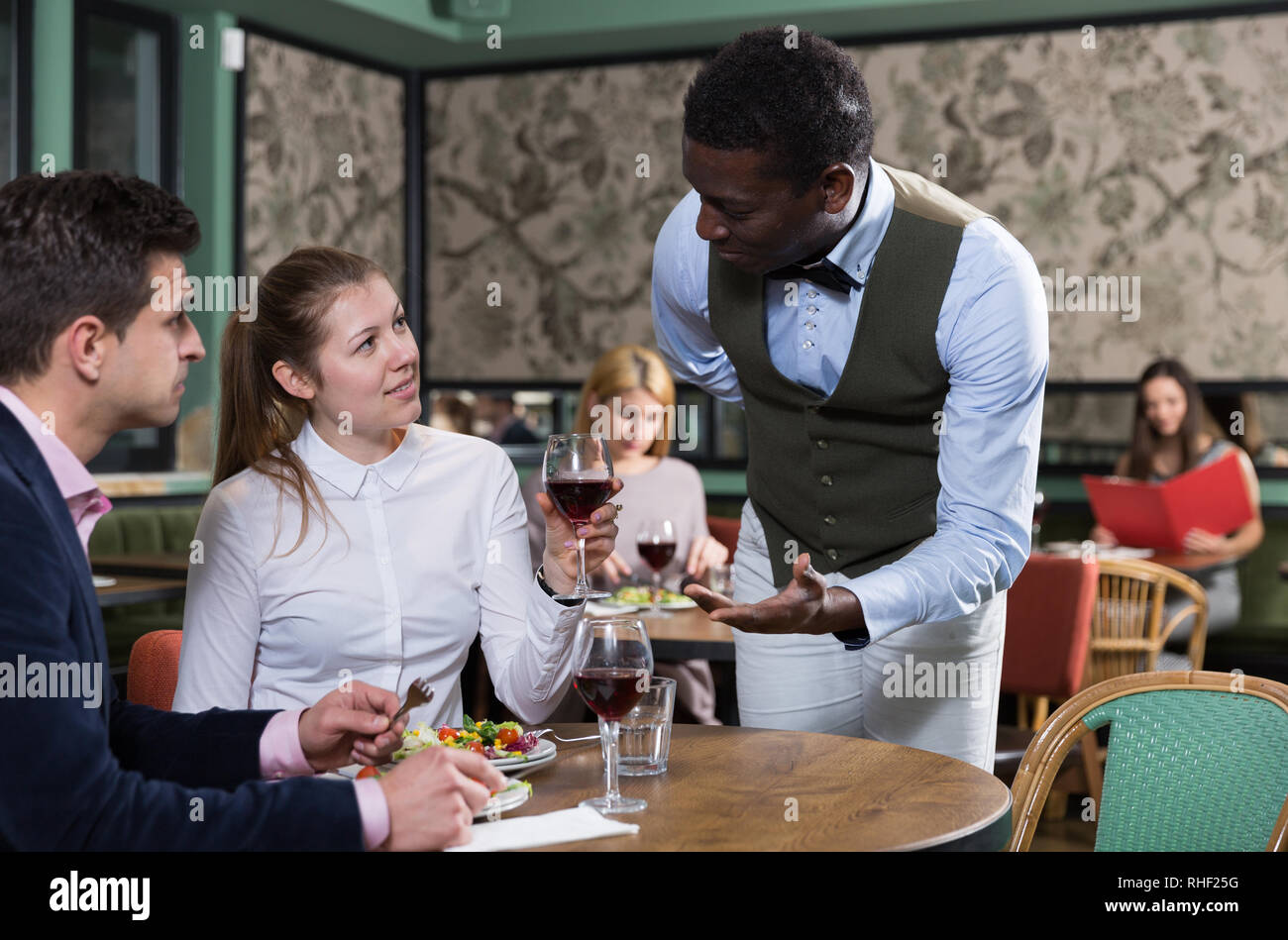 Positive elegant couple talking with polite African American waiter ...