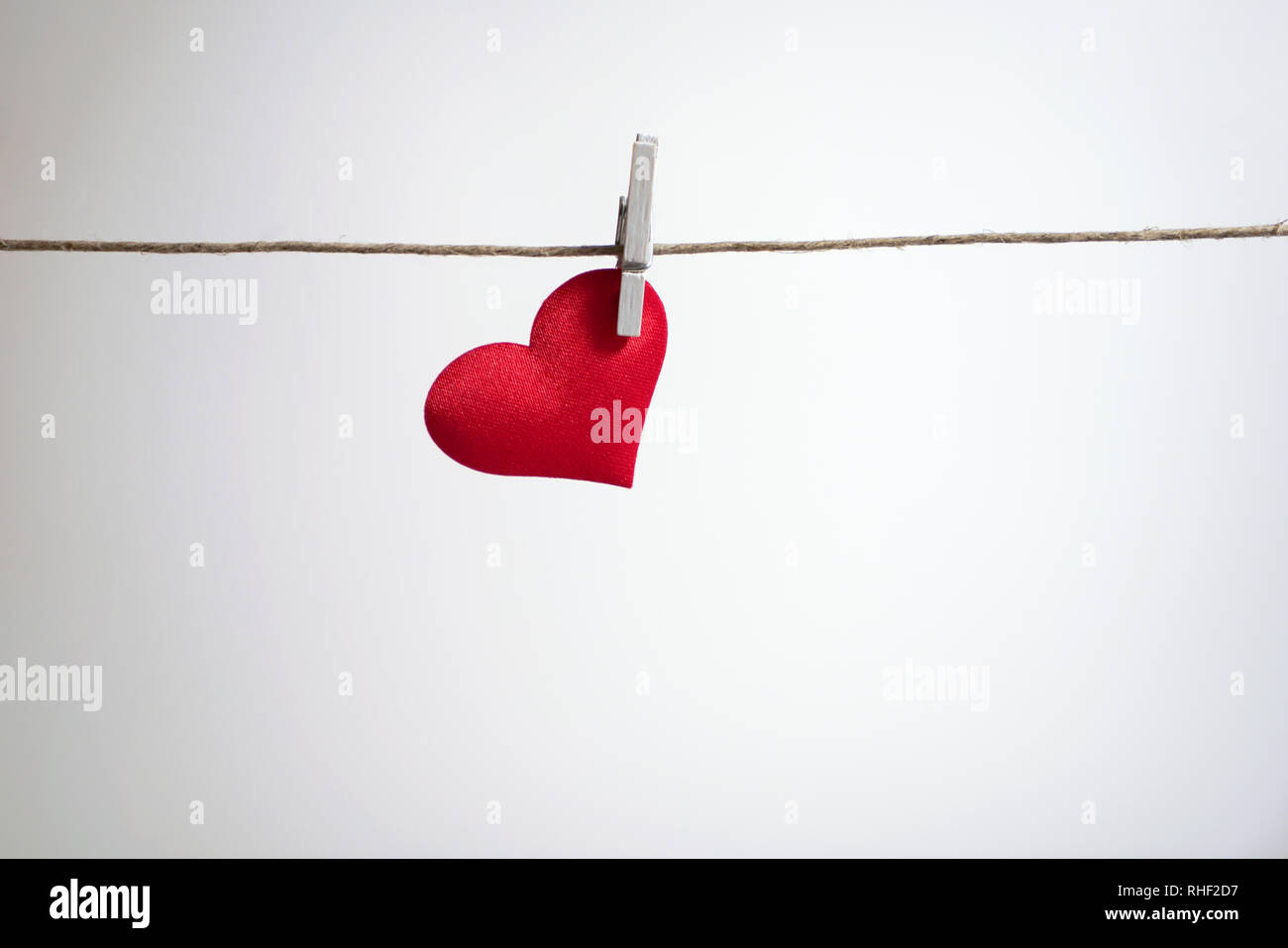 Single red heart hanging from string by clothes peg on white background ...