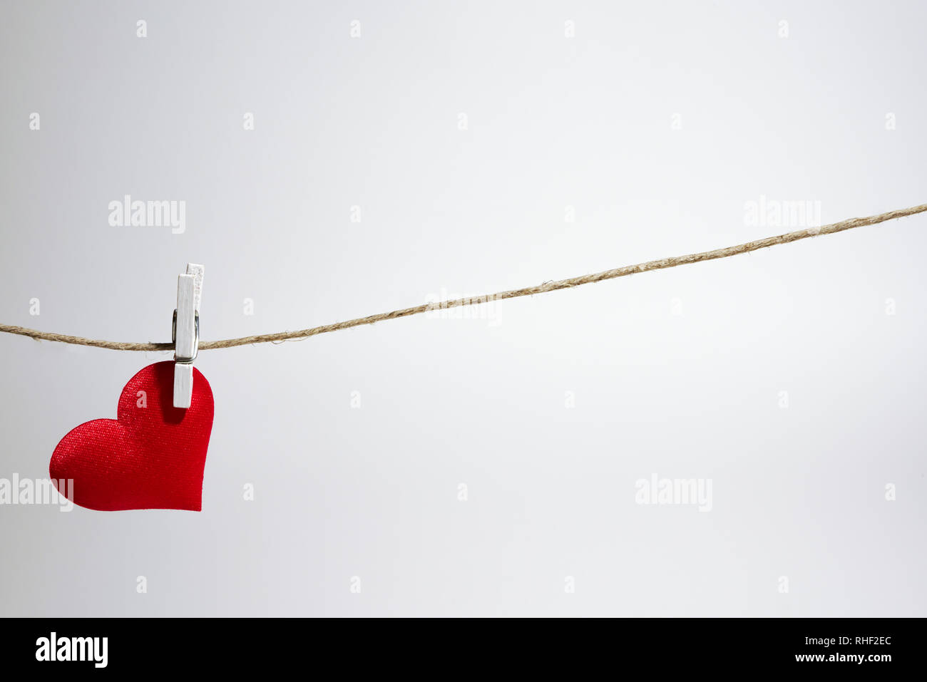 Single lonely red heart hanging from string by clothes peg on white ...