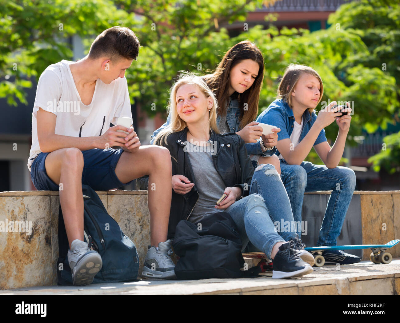 Glad two girls and two boys playing with mobile phones outdoors Stock ...