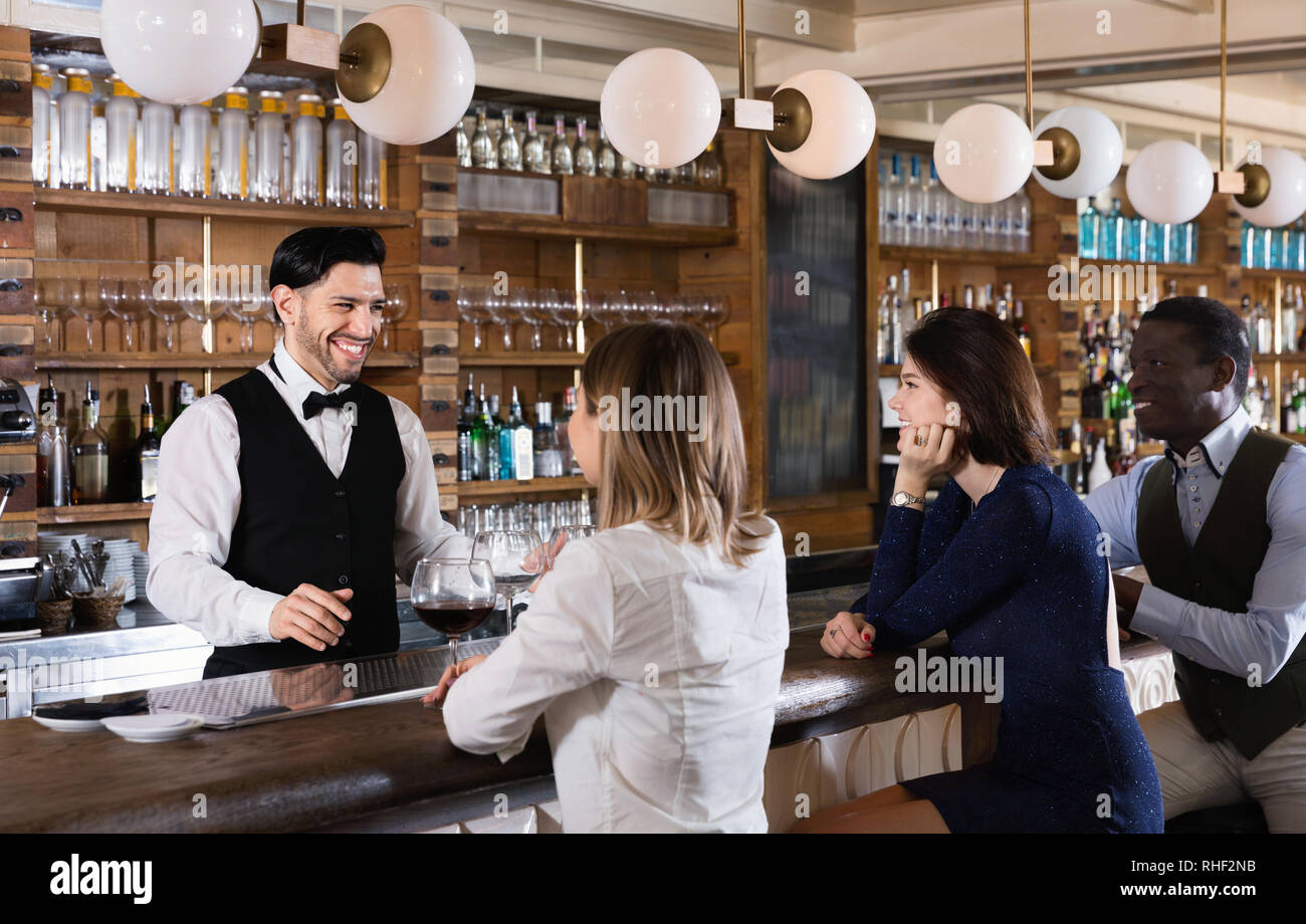Happy cheerful positive smiling barman is servicing young people who ...