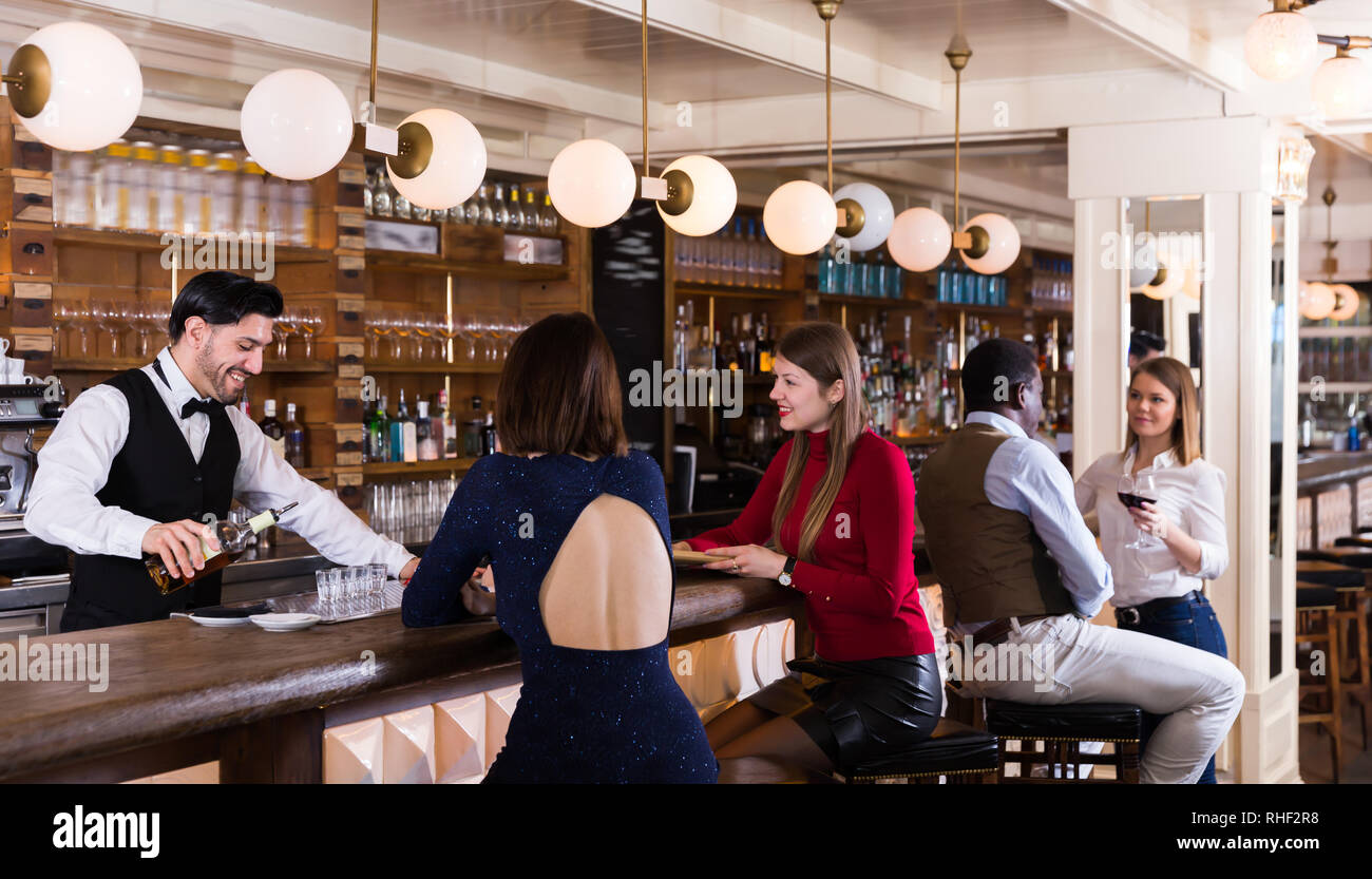 Laughing people are relaxing near bar counter and drinking alcohol in ...