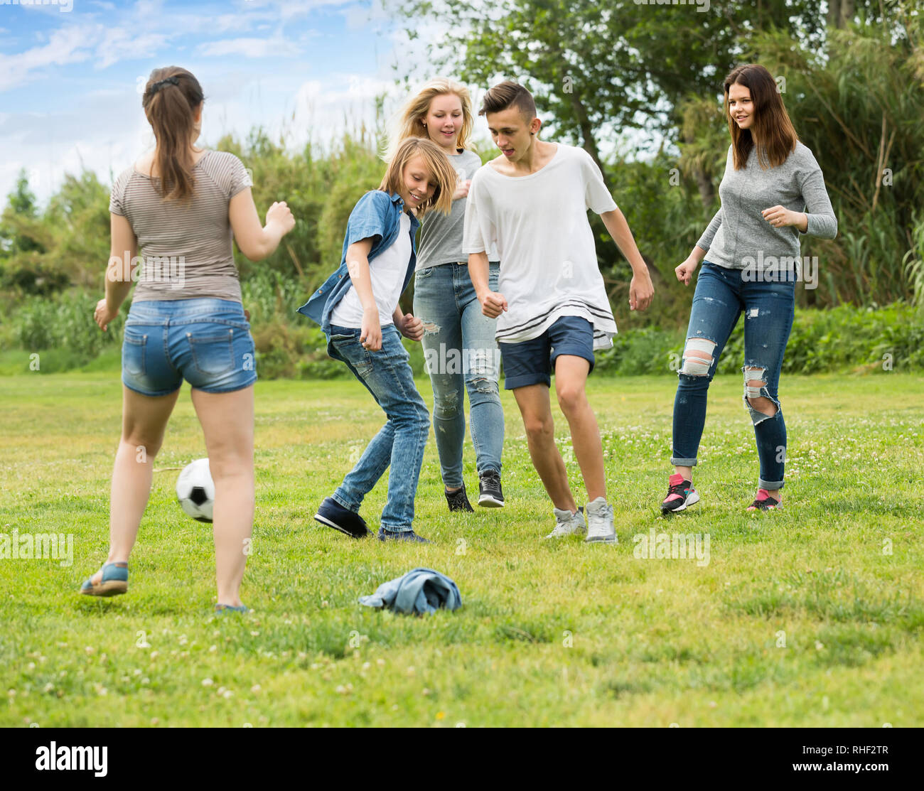 Group of happy teenager friends playing football together on green lawn ...