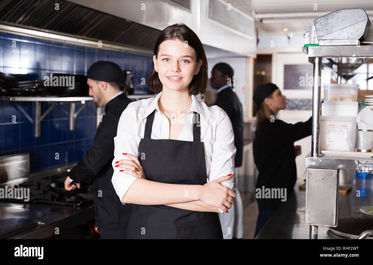 Confident young waitress standing with arms crossed in modern kitchen ...