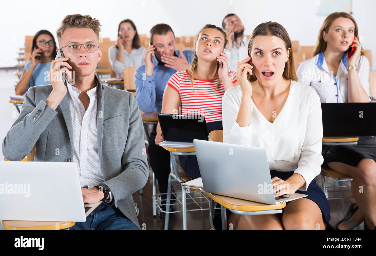Group of young people sitting with laptops in lecture hall, talking on ...