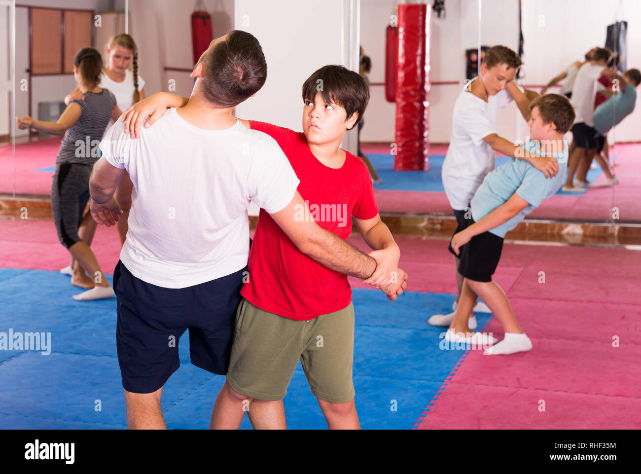 Adult and teen people practicing self defence technique in pairs at gym ...