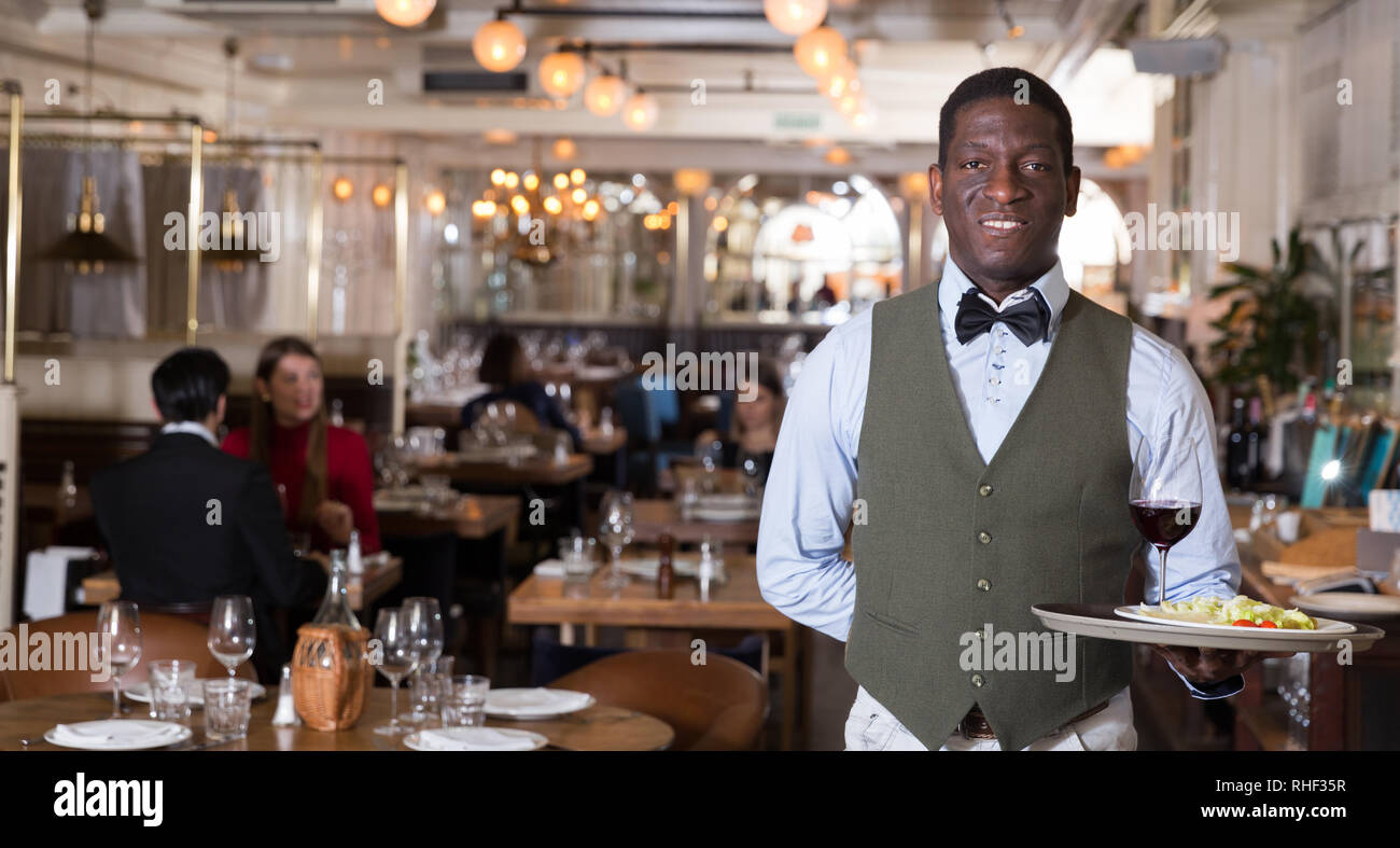 Hospitable African American waiter standing with serving tray ...