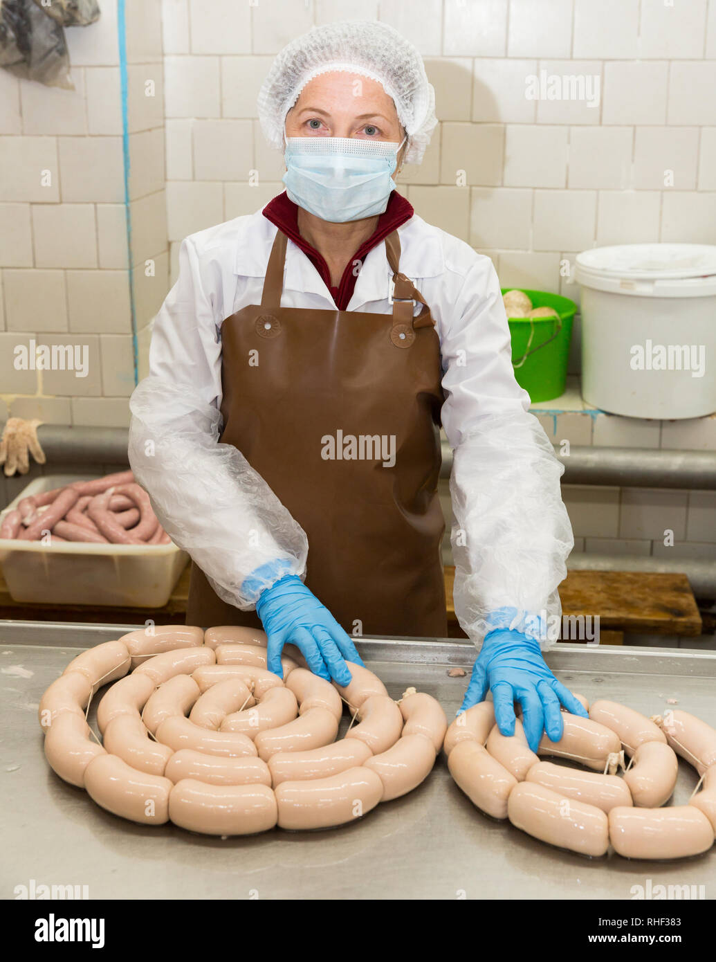 Focused mature woman filling and forming sausages at food production ...