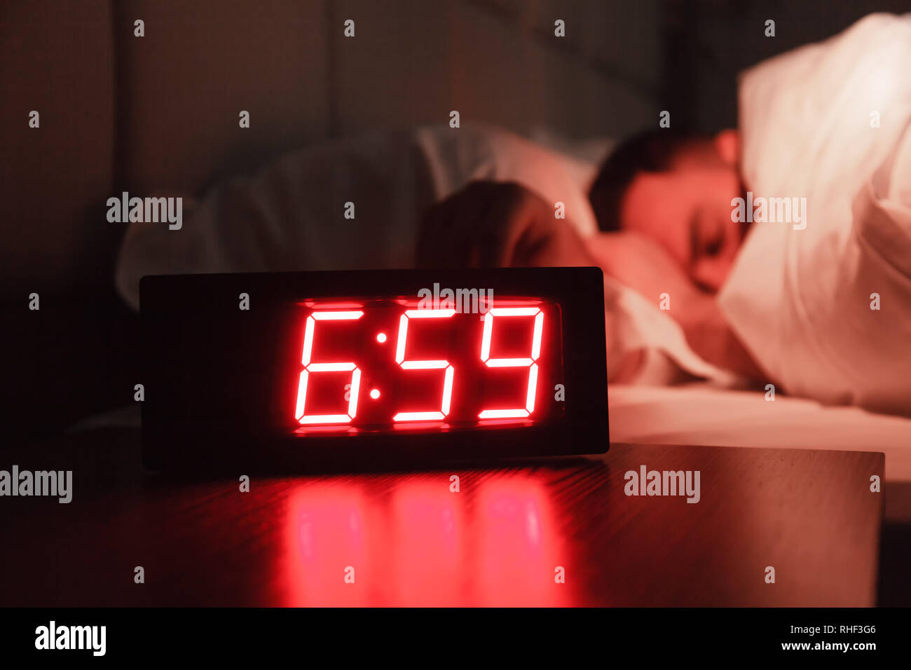 Alarm clock on the bedside table with red numbers, sleeping man in bed ...