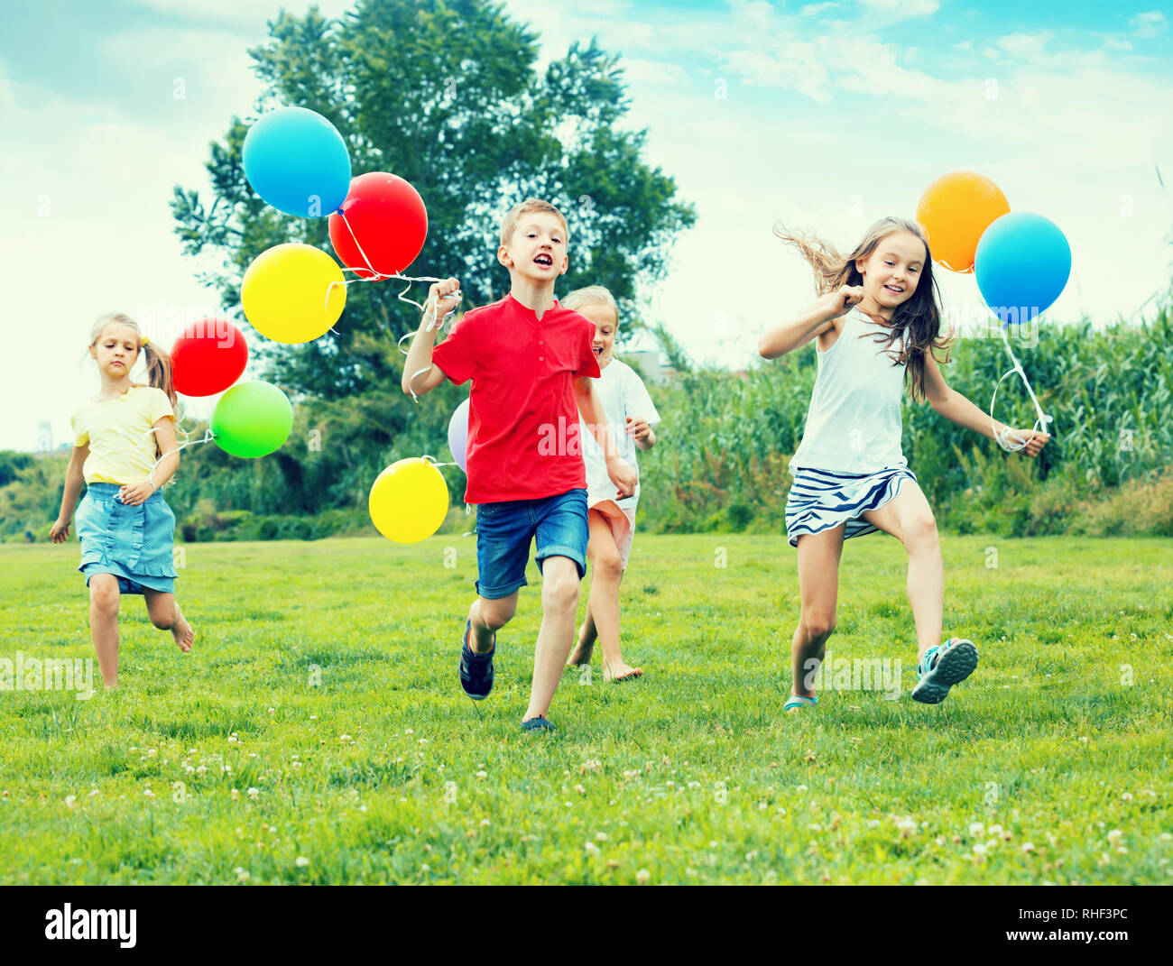 Four friendly glad kids happily playing and running together on green ...