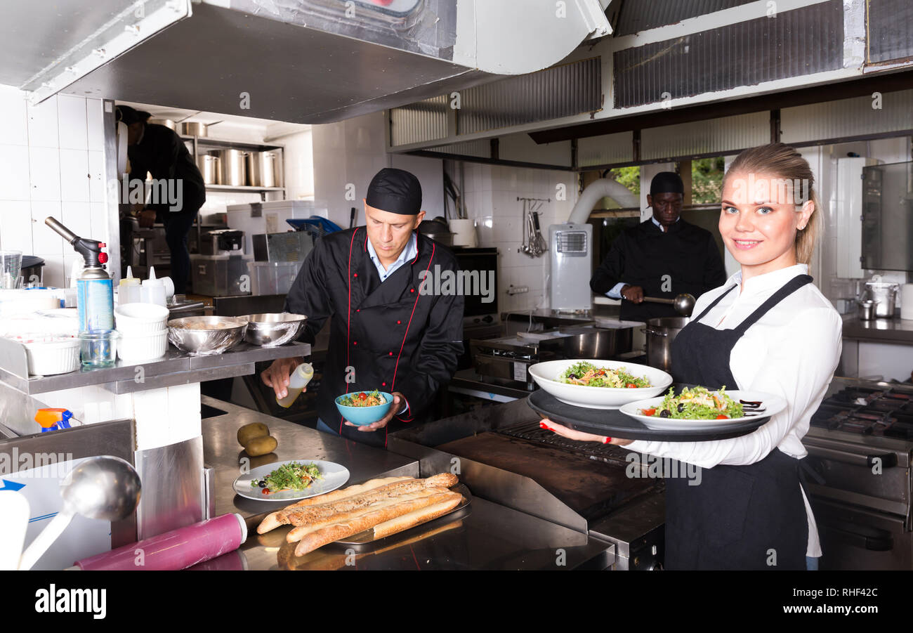 Smiling young waitress holding delicious cooked meals in restaurant ...