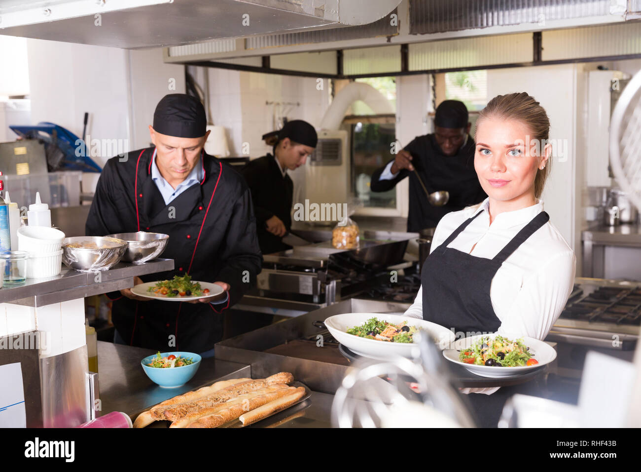 Portrait of attractive waitress with ordered dishes in kitchen of ...