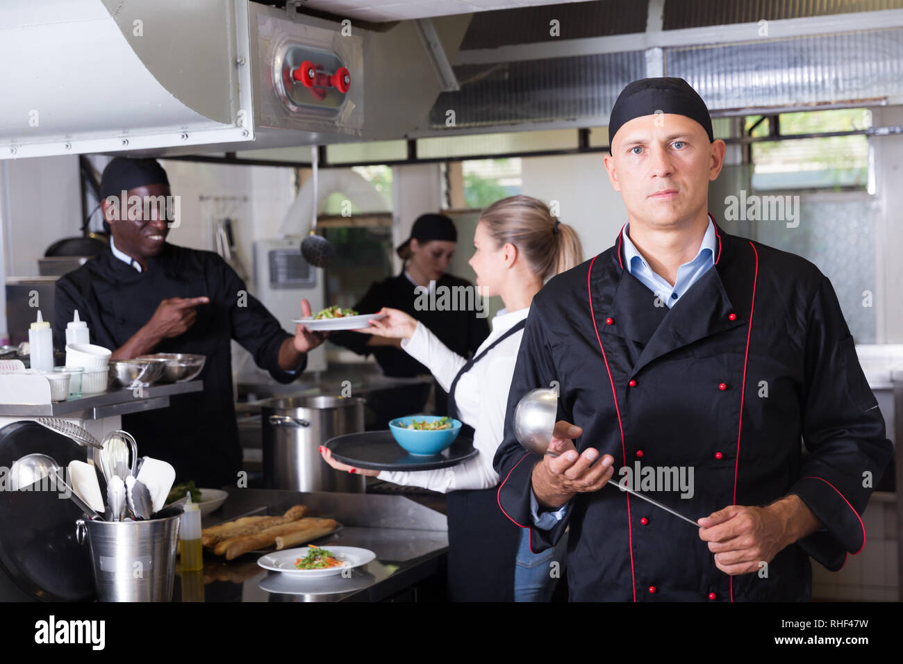 Portrait of confident male chef in restaurant kitchen with busy ...