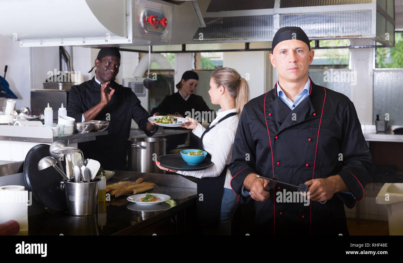 Portrait of confident male chef in restaurant kitchen with busy ...