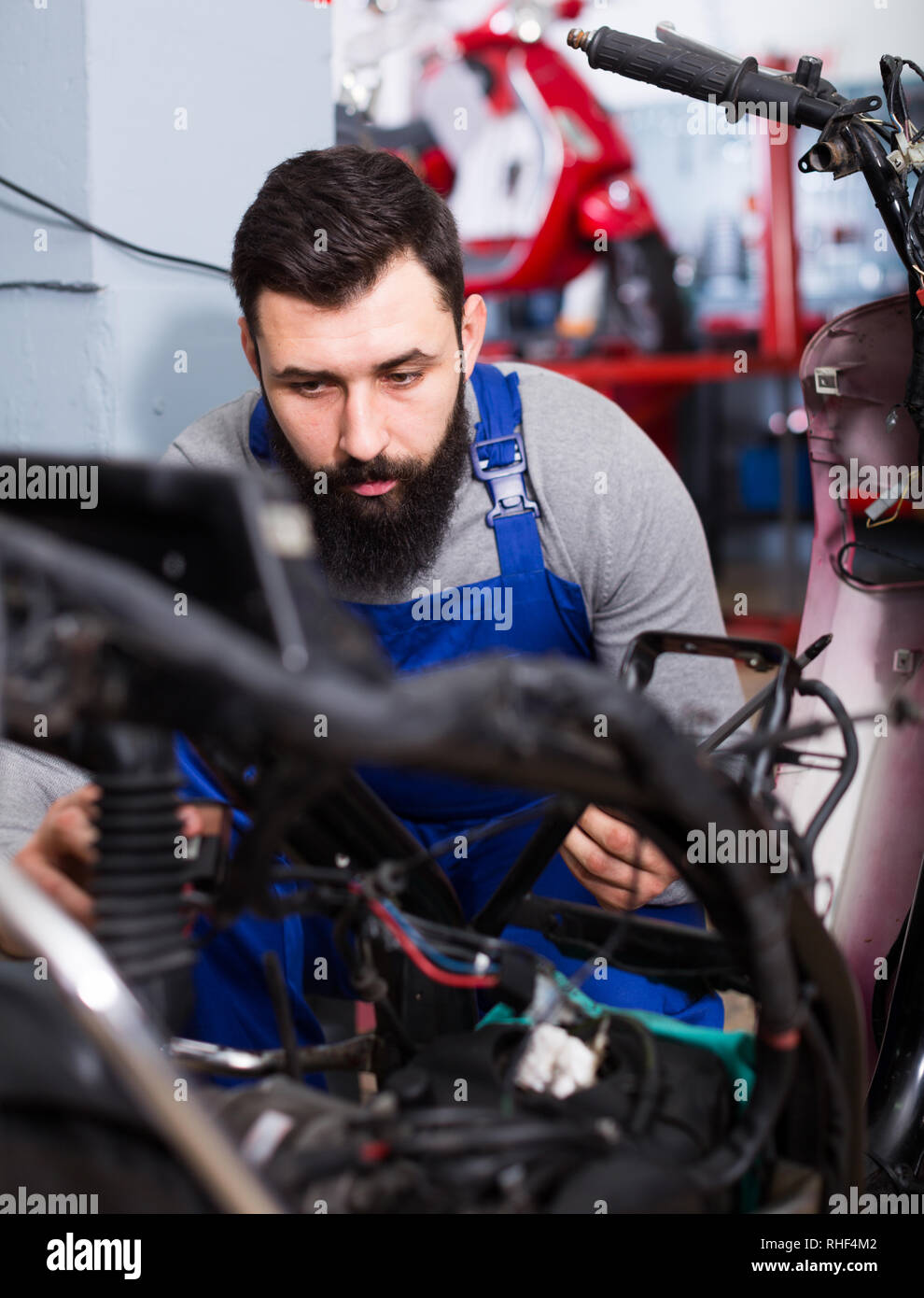 Smiling male worker fixing failed motorcycle in motorcycle workshop ...