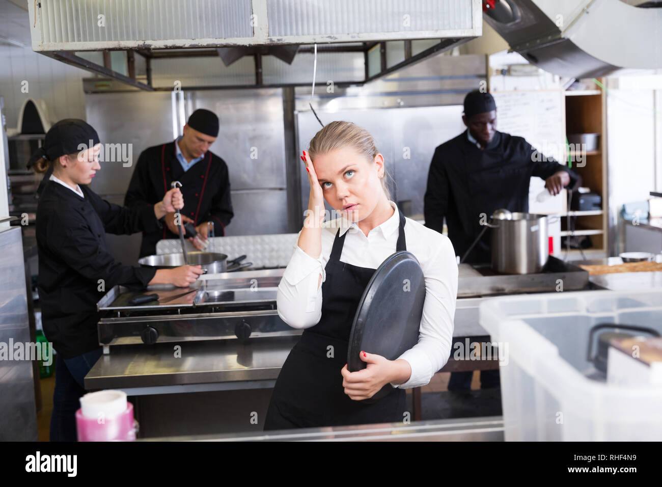 Unhappy and tired young waitress waiting ordered dishes in restaurant ...