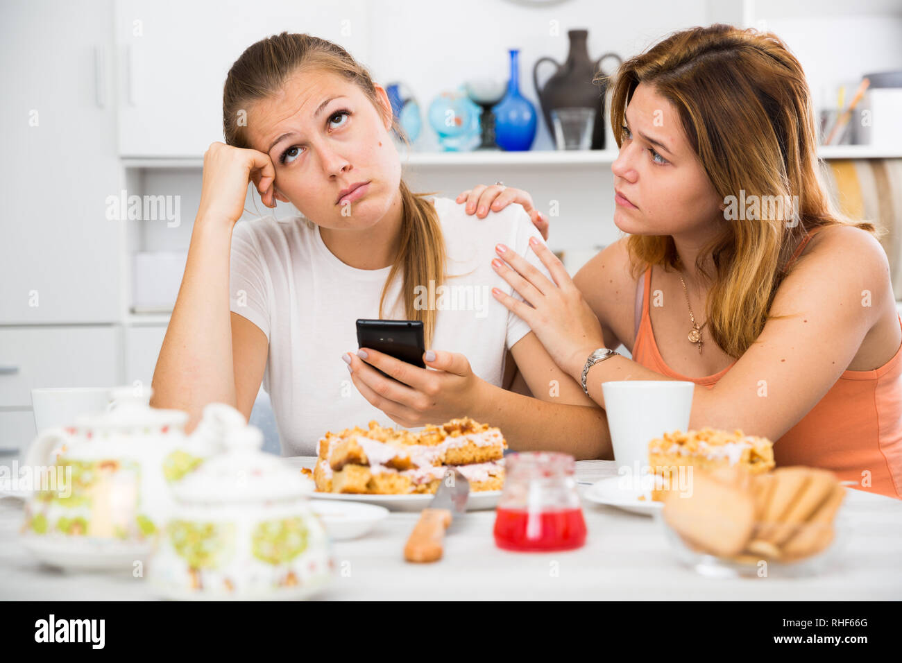 Portrait of female talking with sad girl friend with mobile at the ...