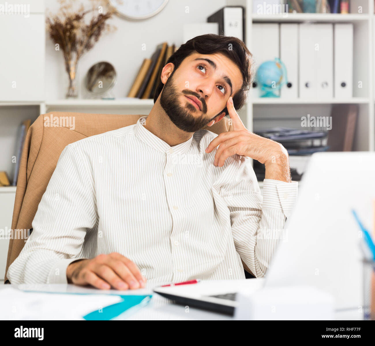 Portrait of handsome brunette manager having thoughtful look at office ...