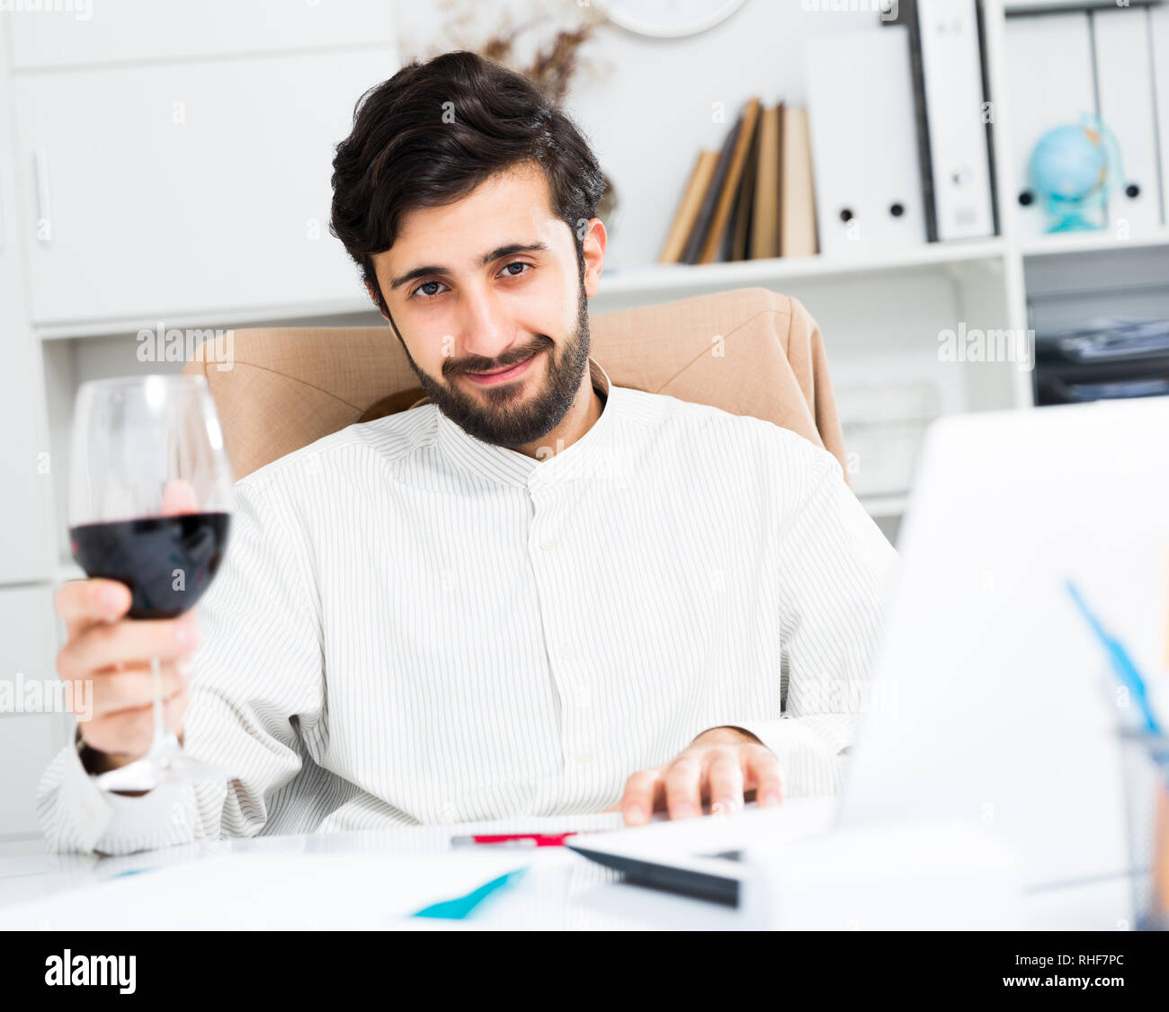 Handsome young office worker drinking red wine at office desk Stock ...