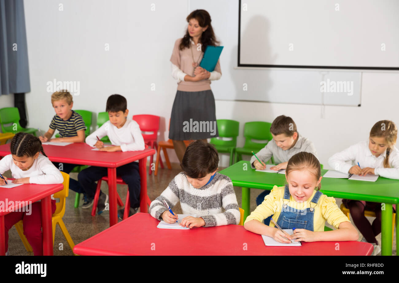 Assiduous school kids with pens and notebooks studying in classroom ...