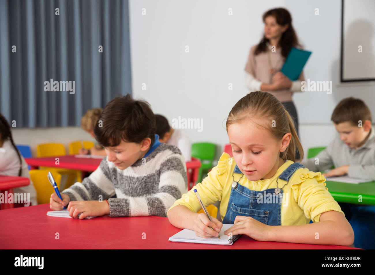Assiduous school kids with pens and notebooks studying in classroom ...