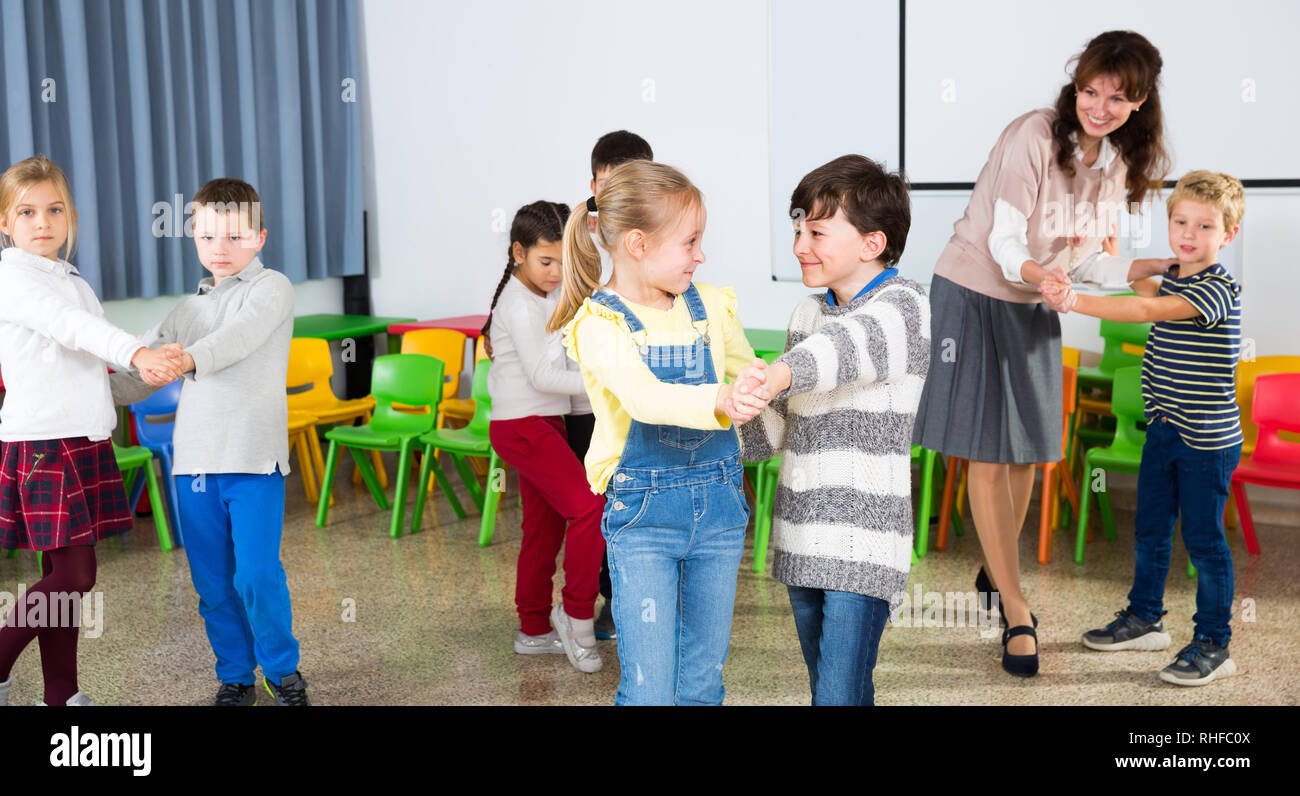 Happy kids and female teacher dancing together in classroom at ...