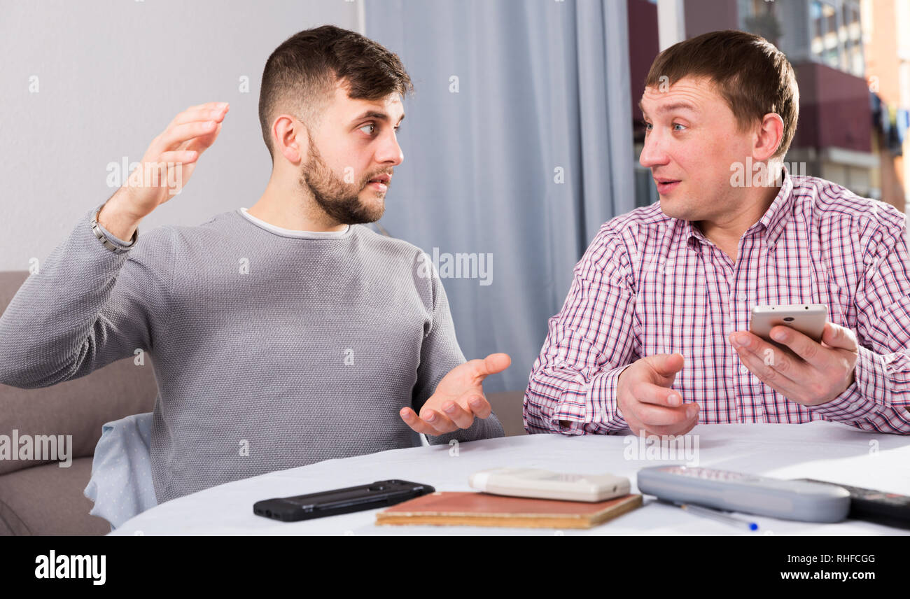 Two cheerful men talking and laughing while enjoying beer at home ...