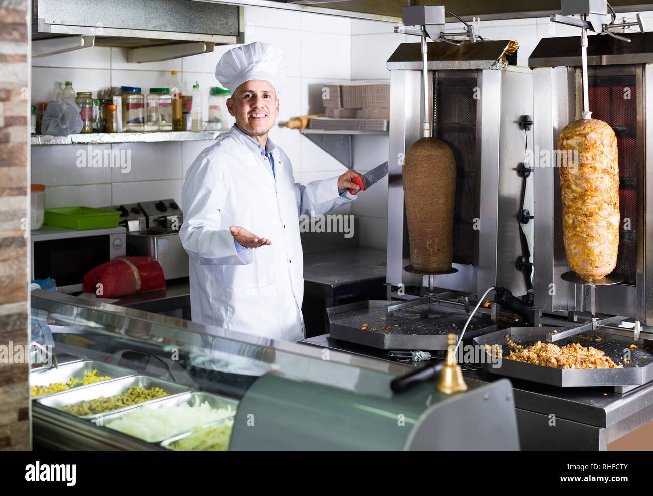 smiling american mature man chef wearing uniform cutting meat for kebab ...