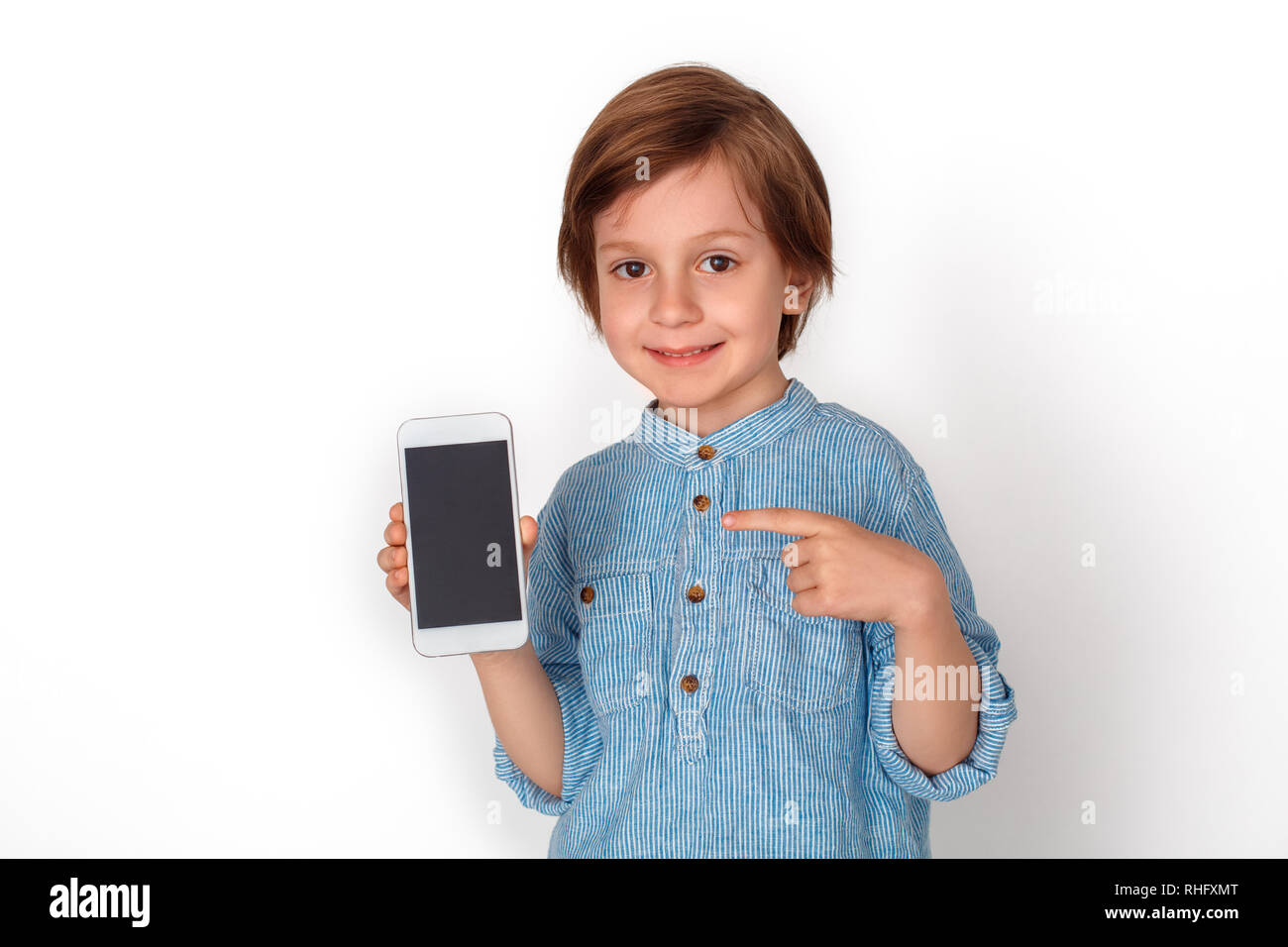 Little boy studio standing isolated on grey wall pointing at smartphone ...