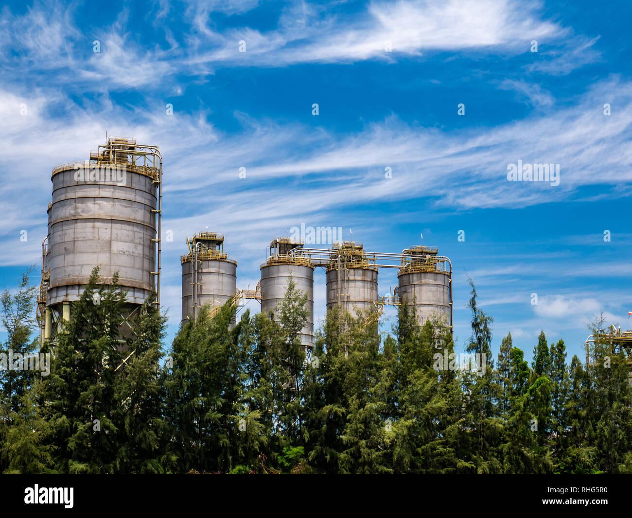 Chemical powder silos behind row of tree with blue sky, Thailand Stock ...