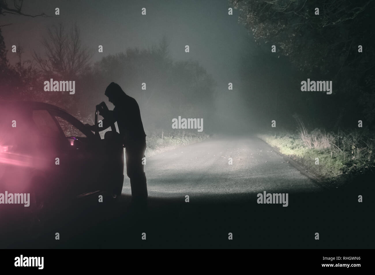 A lone hooded figure looking into a car. Silhouetted on a spooky ...