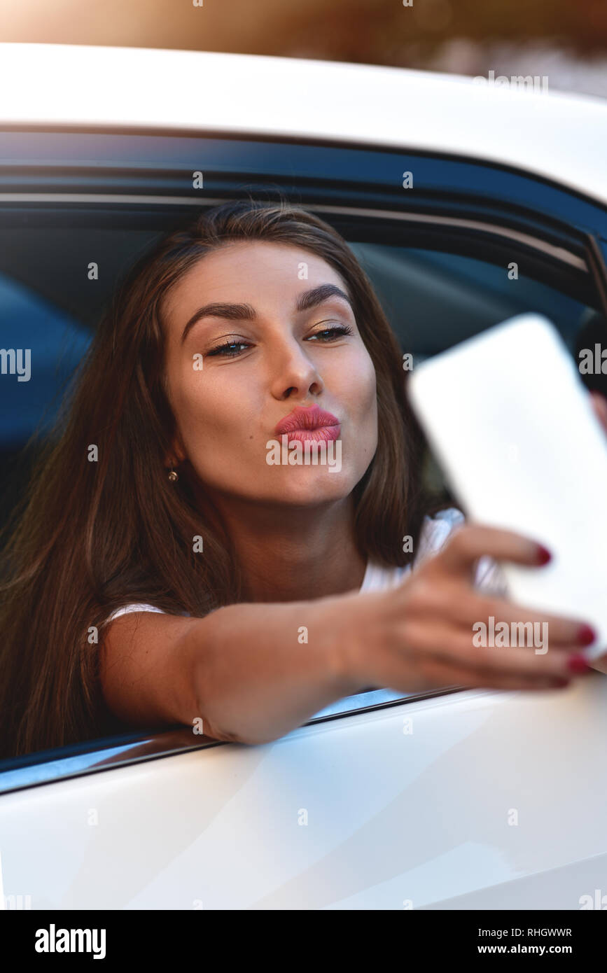 Young woman in the car going on holiday as a passenger makes selfie ...