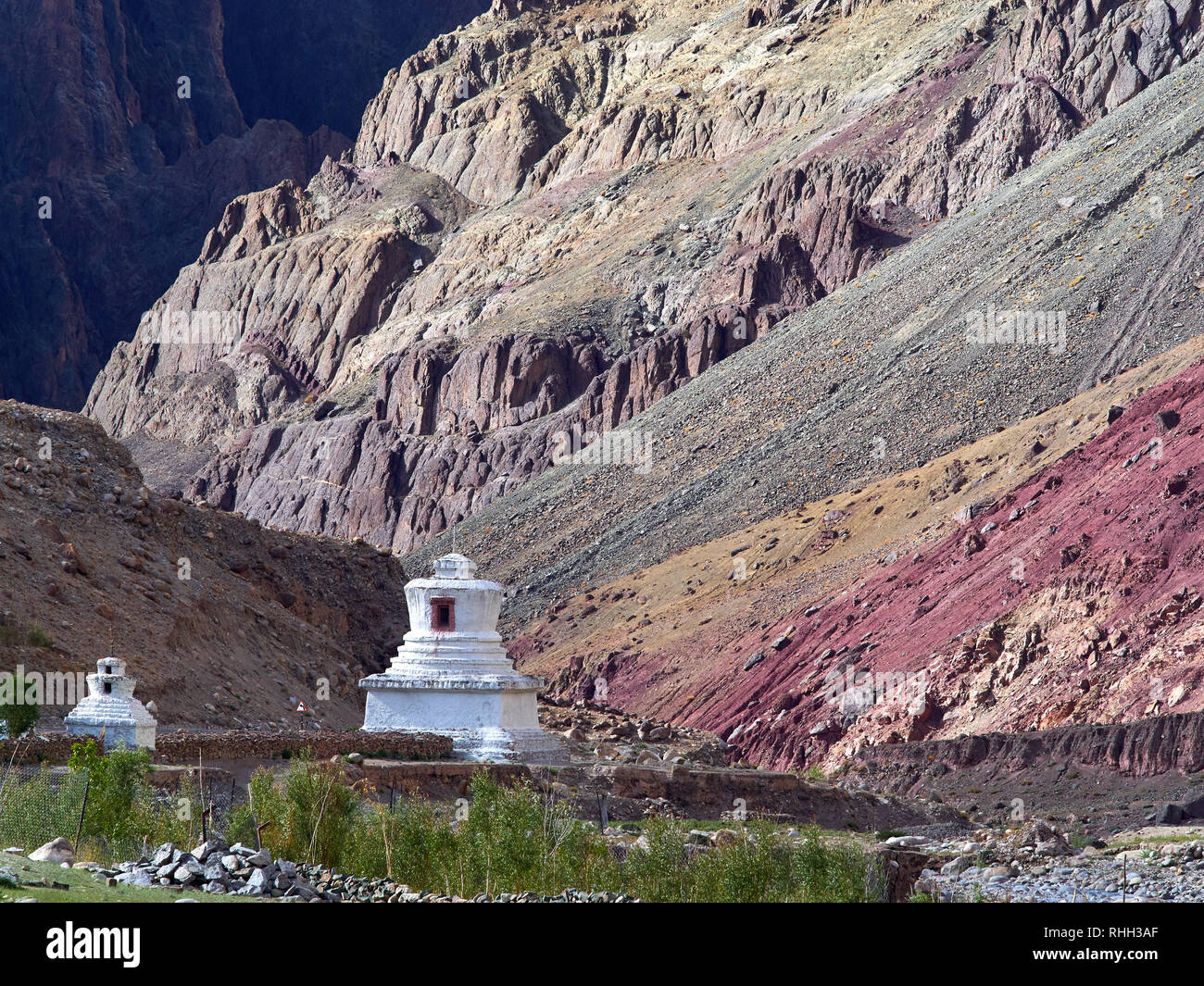 White Buddhist stupas, chortens of stone, among the red mountain gorge ...