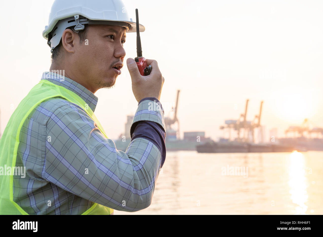 Asian harbor dock worker talking on radio with ship background - Image ...