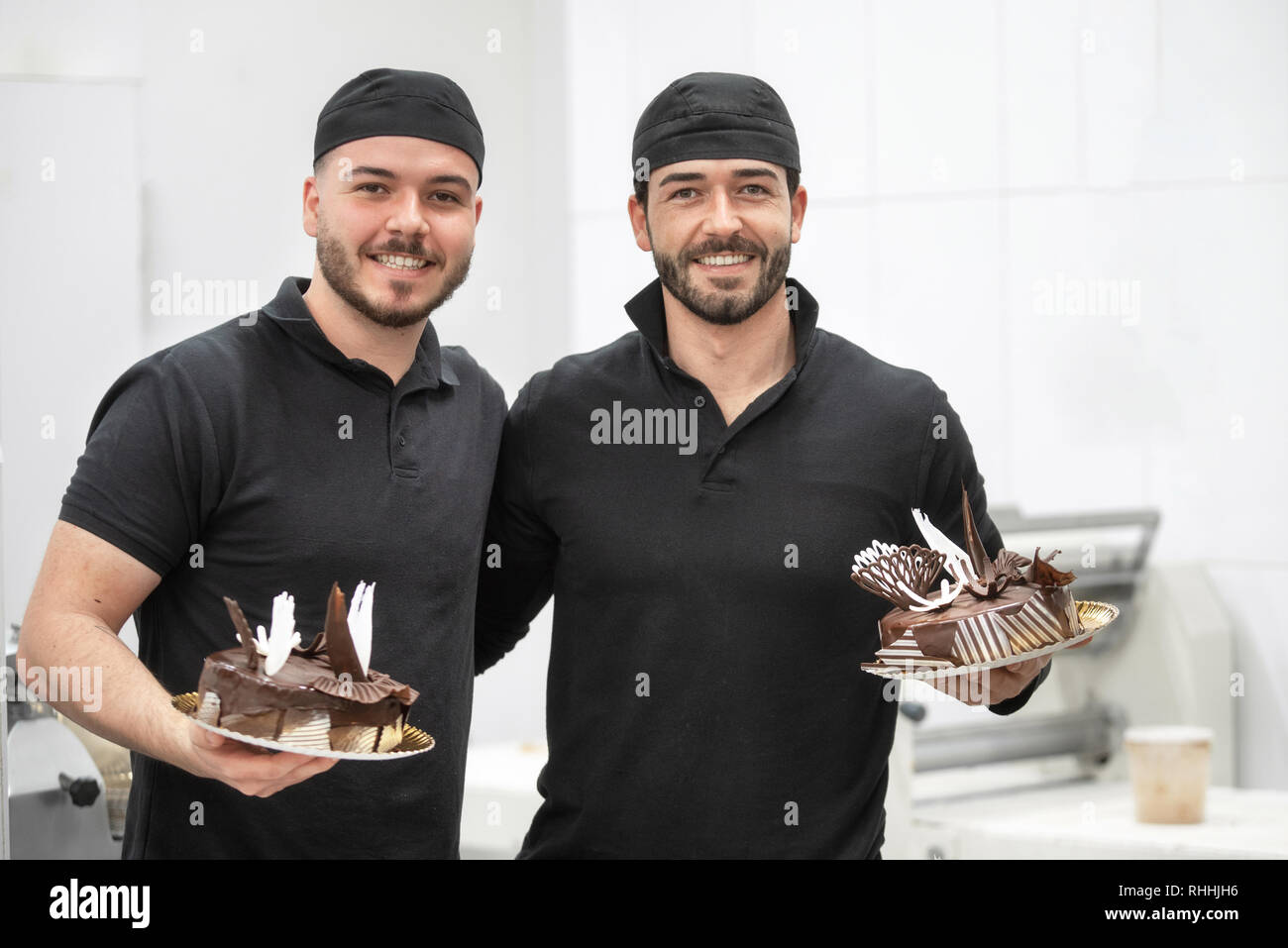 Portrait of two pastry chefs smiling with cakes in his hands, working ...