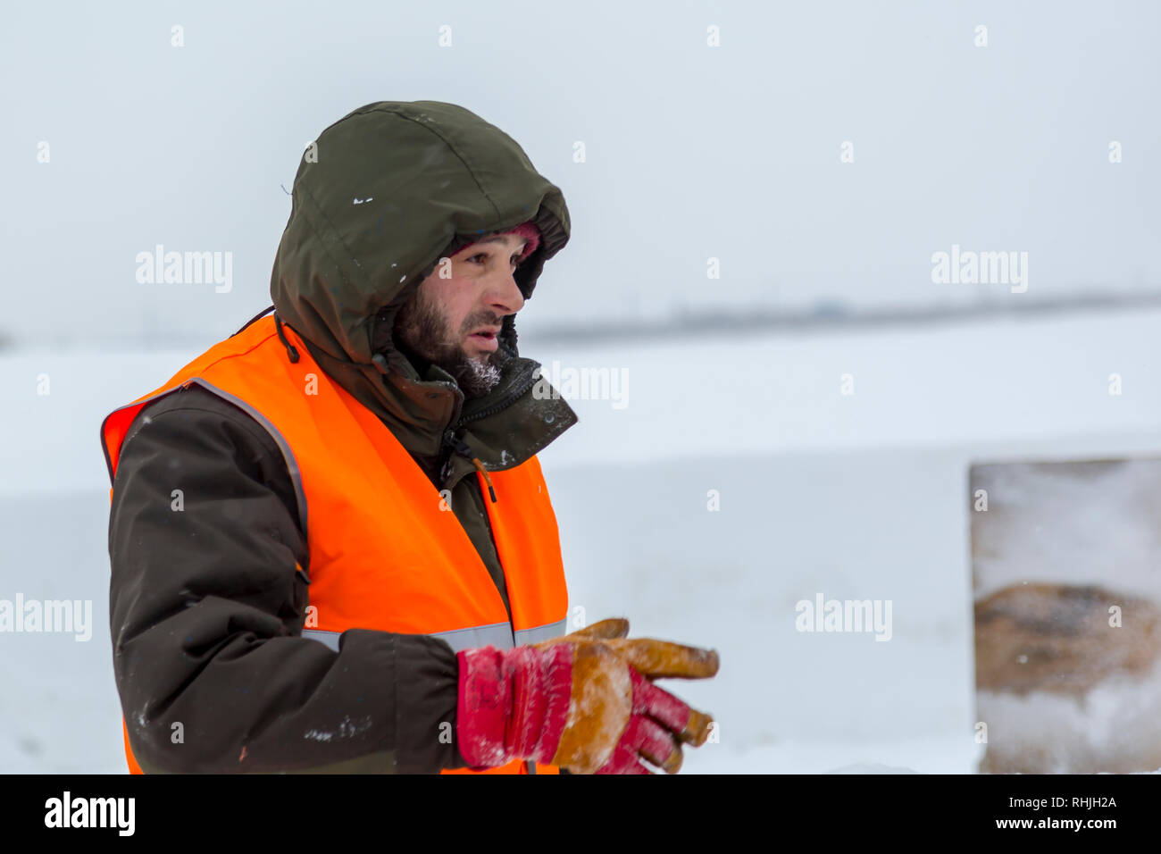 Worker in a green jacket with a hood and a reflective vest at the ...
