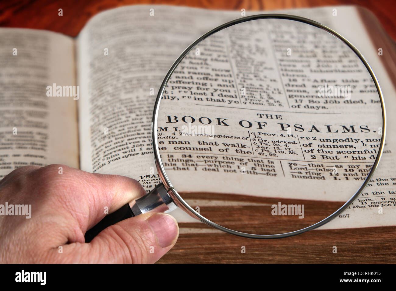 Hand holding magnifying glass over an old Bible opened to the famous ...