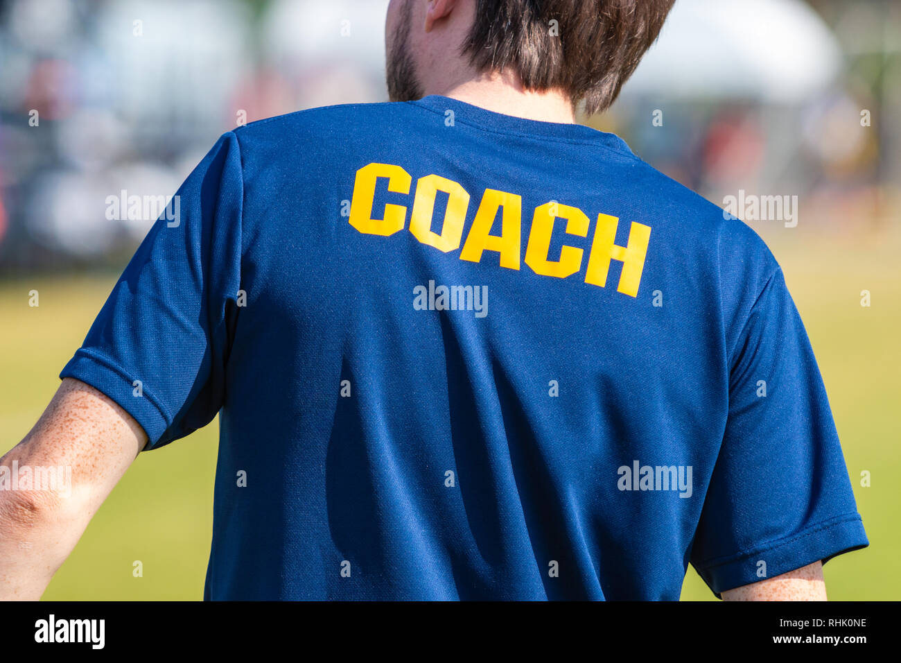 Back of male sport coach wearing blue shirt with COACH yellow text on ...