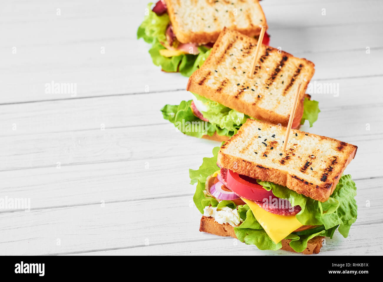 Three sandwiches with ham, lettuce and fresh vegetables on white ...