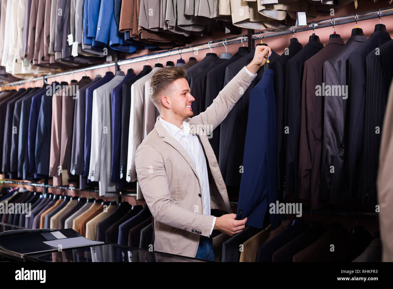 smiling male customer examining suits in men’s cloths store Stock Photo ...