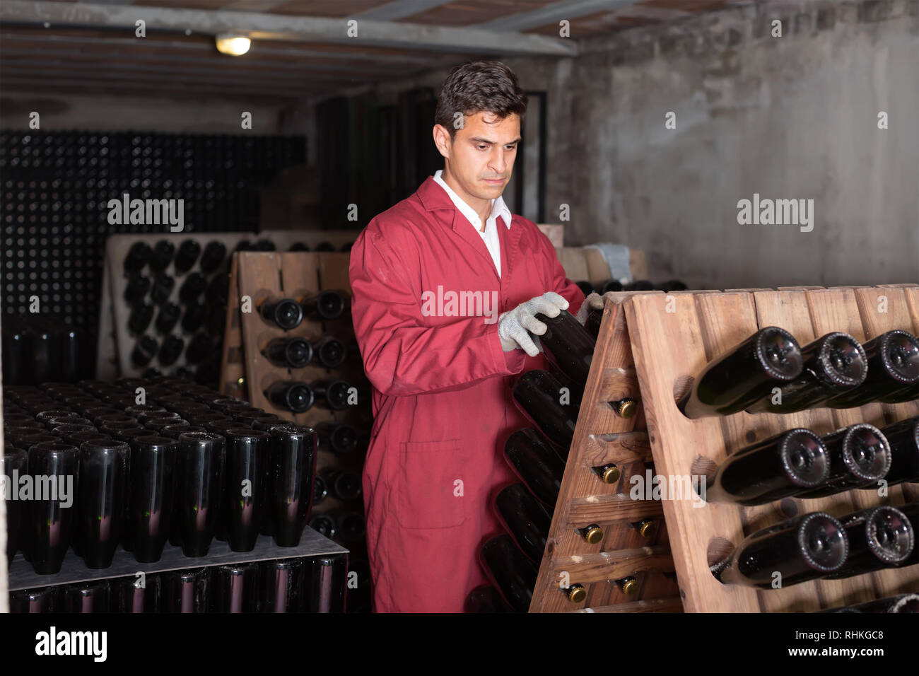 man wearing uniform working with bottle storage racks in winery cellar ...