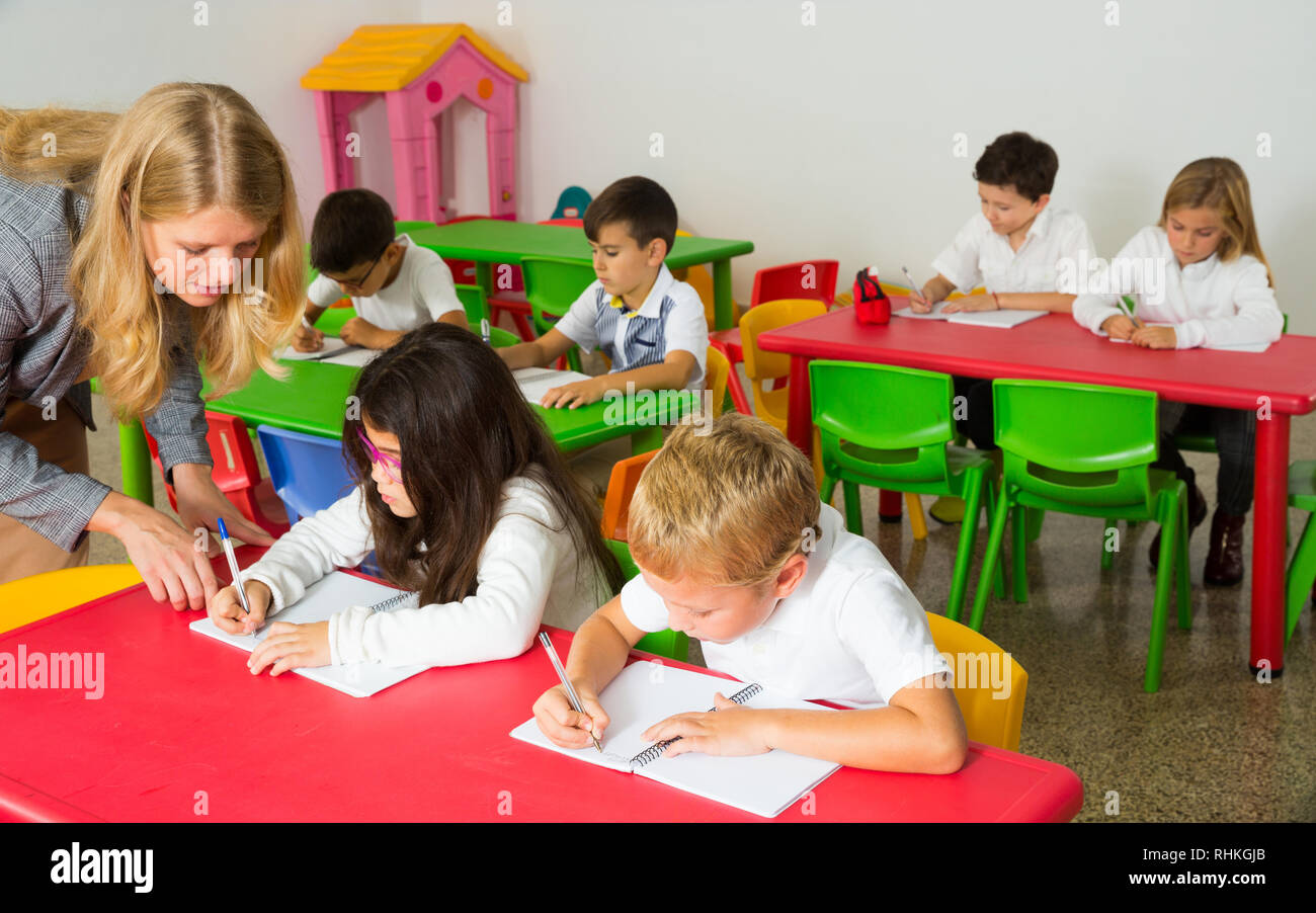 Female teacher helping schoolchildren doing their task in classroom ...