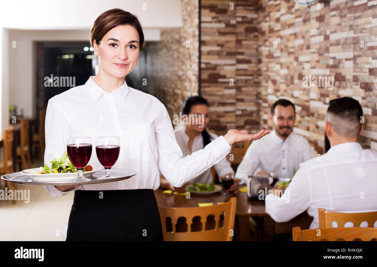 Glad female waiter welcoming guests to country restaurant Stock Photo ...