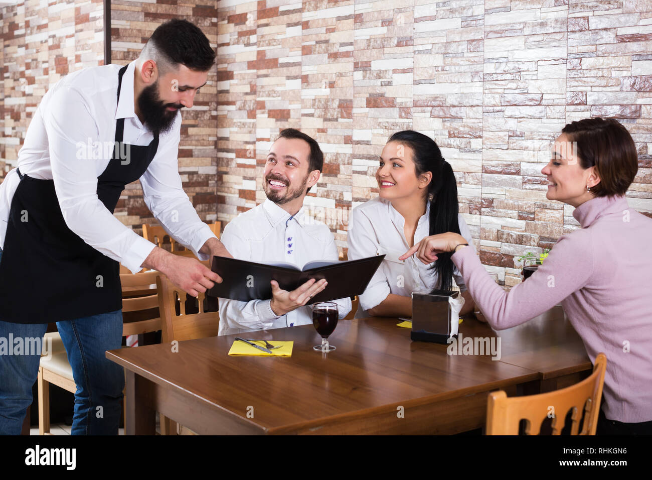 Positive male waiter taking order from visitors in country restaurant ...