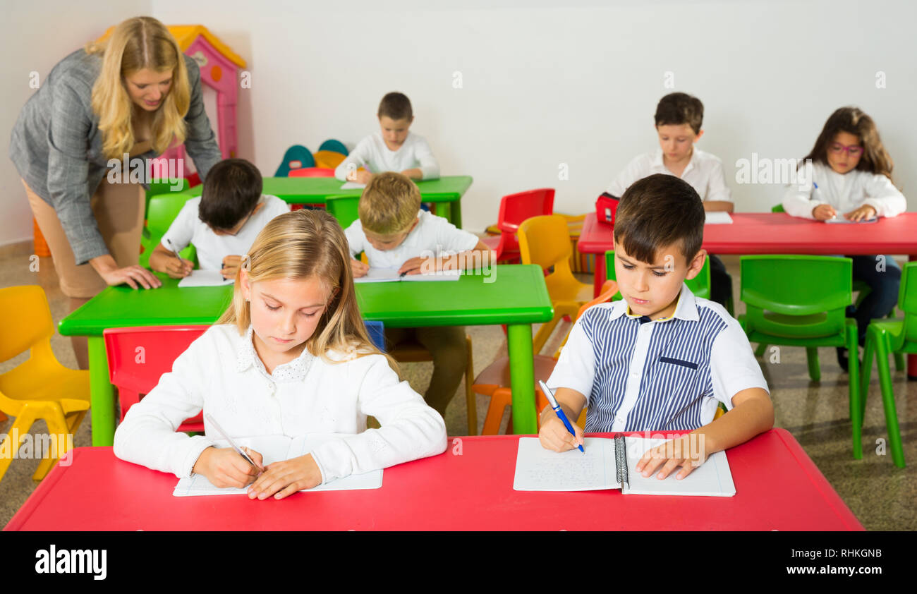 Little diligent schoolkids and their female teacher working at ...
