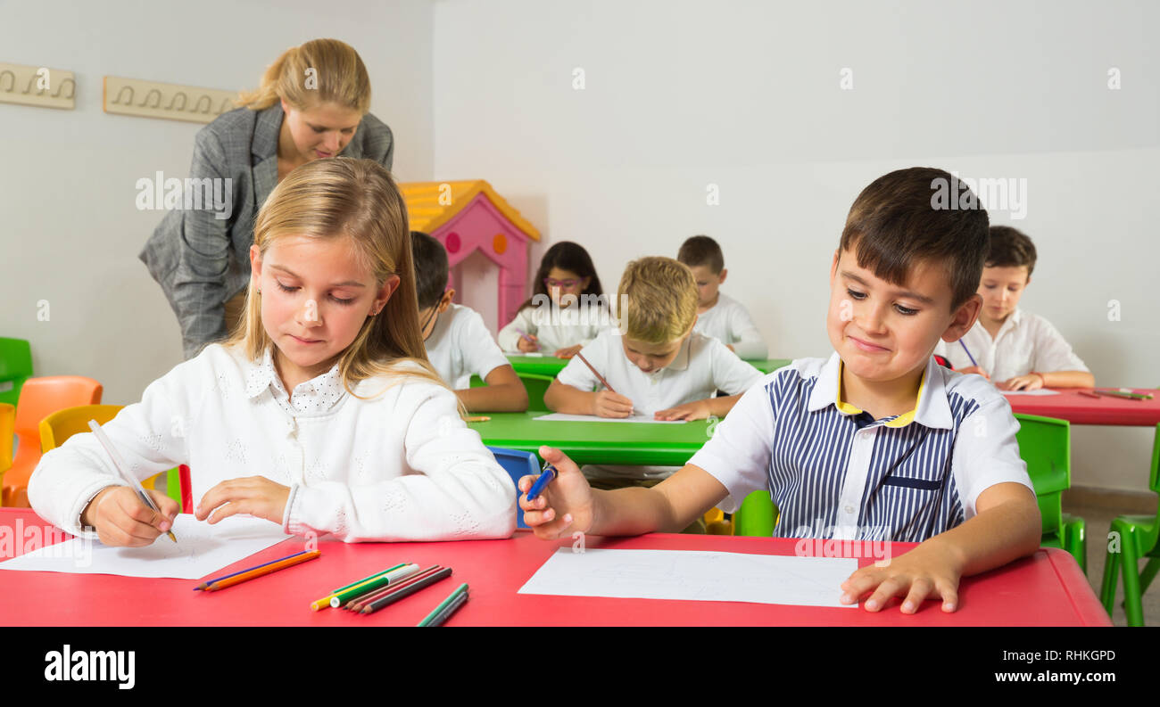 Portrait of two schoolkids and their teacher helping children in ...