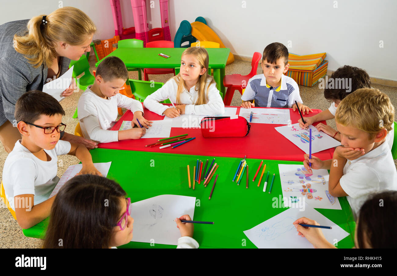 Positive female teacher helping schoolkids drawing with color pencils ...