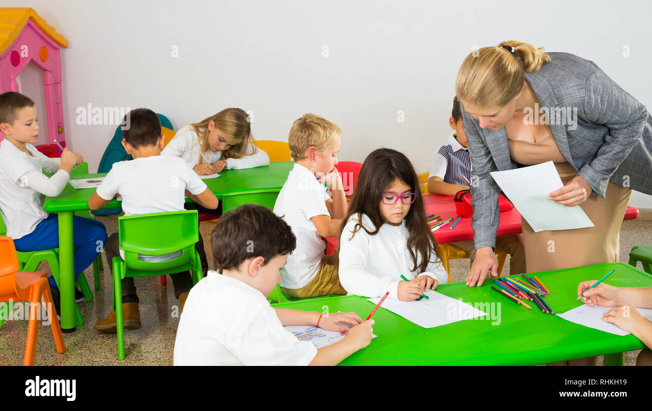 Group of school kids with pens and notebooks studying in classroom with ...