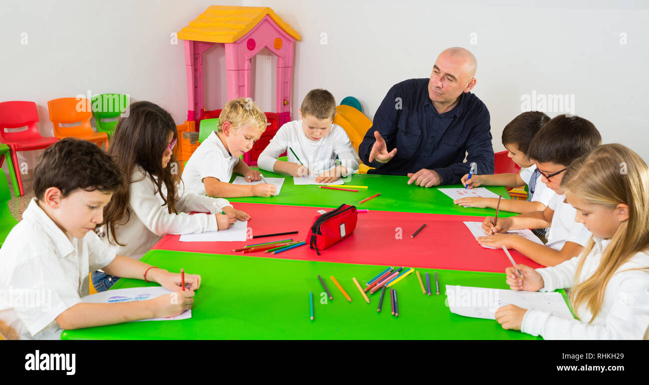 Group of diligent schoolkids drawing with cheerful male teacher at ...