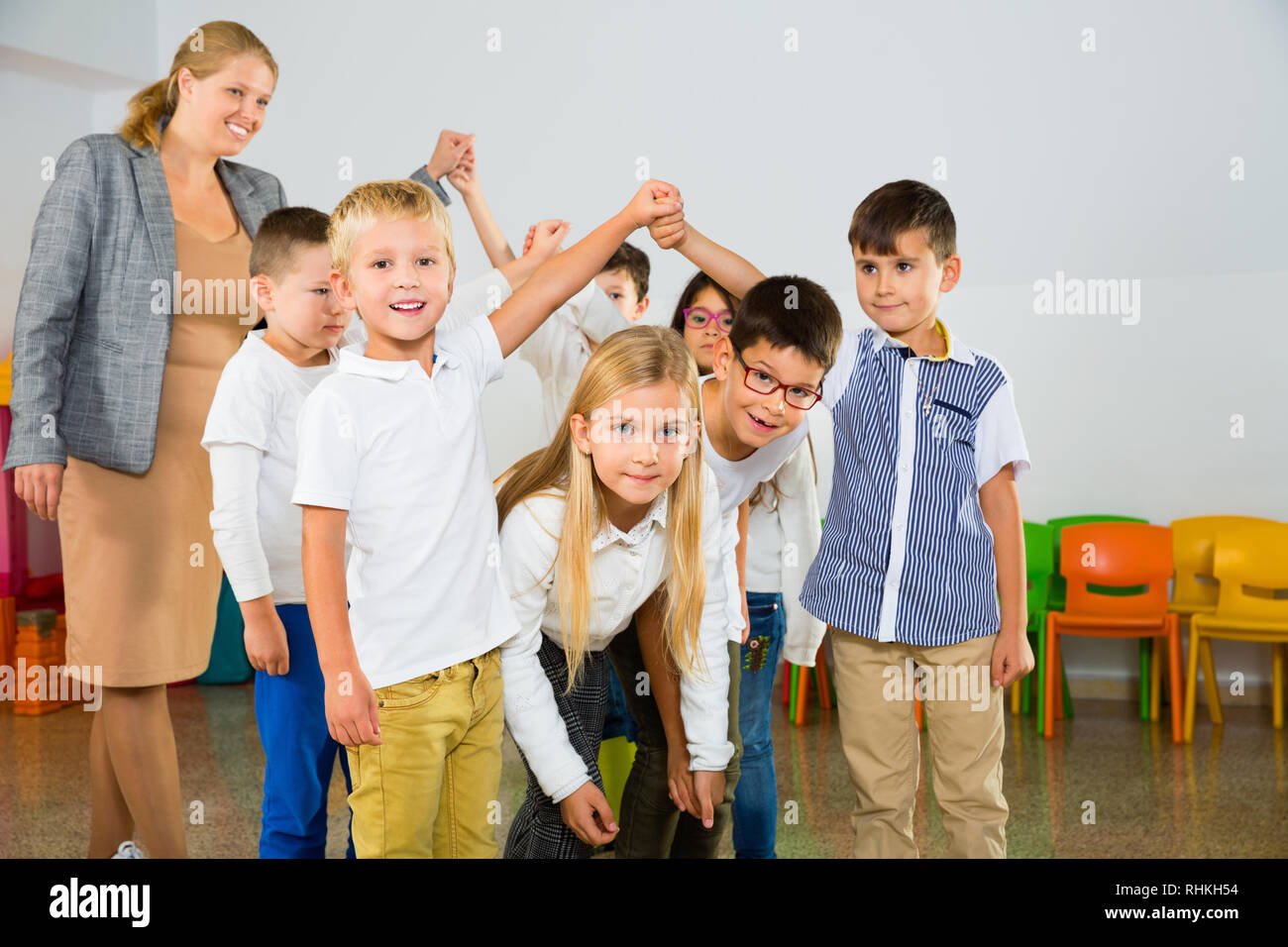 Positive happy cheerful smiling female teacher playing circle game with children in classrom ...